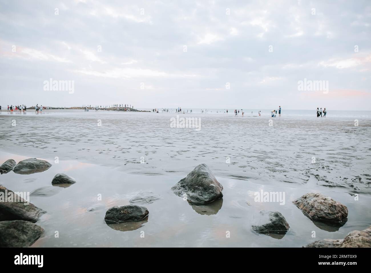 Rocks on the puddle of the beach while low tide with many people in the ...