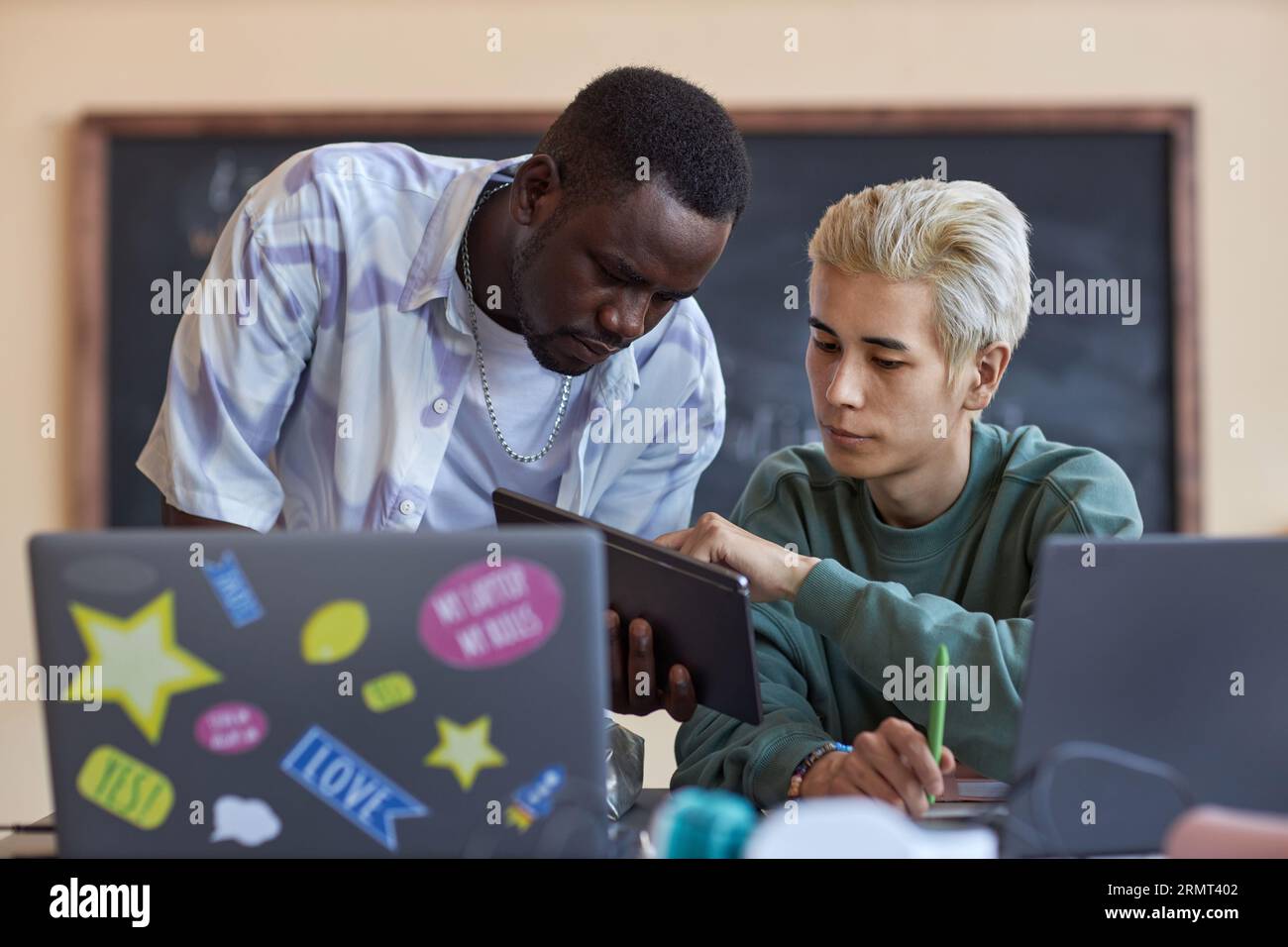 African American guy looking at screen of tablet held by his classmate ...
