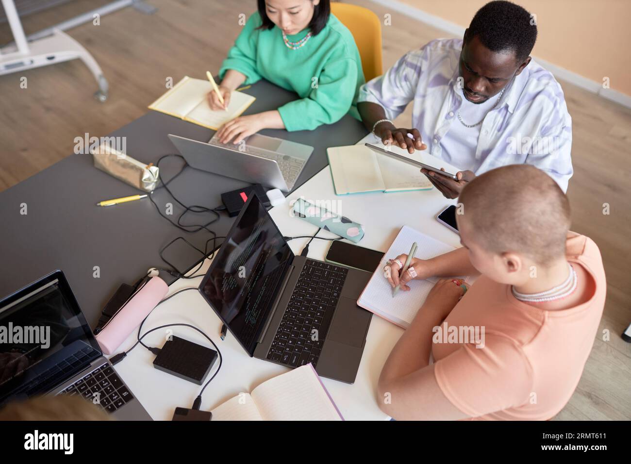 Above angle of intercultural students making notes and using mobile ...