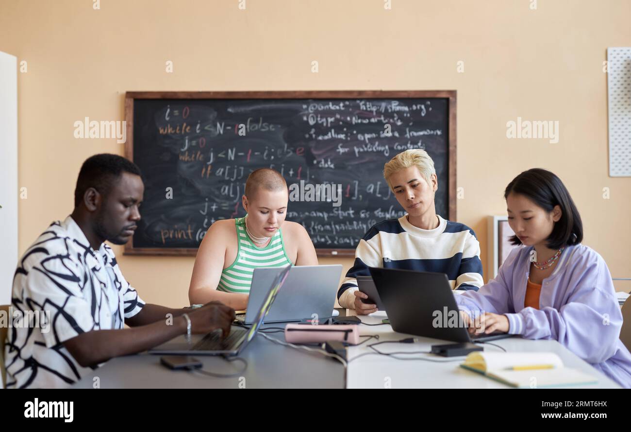Four young intercultural coworkers in casualwear looking at screens of ...