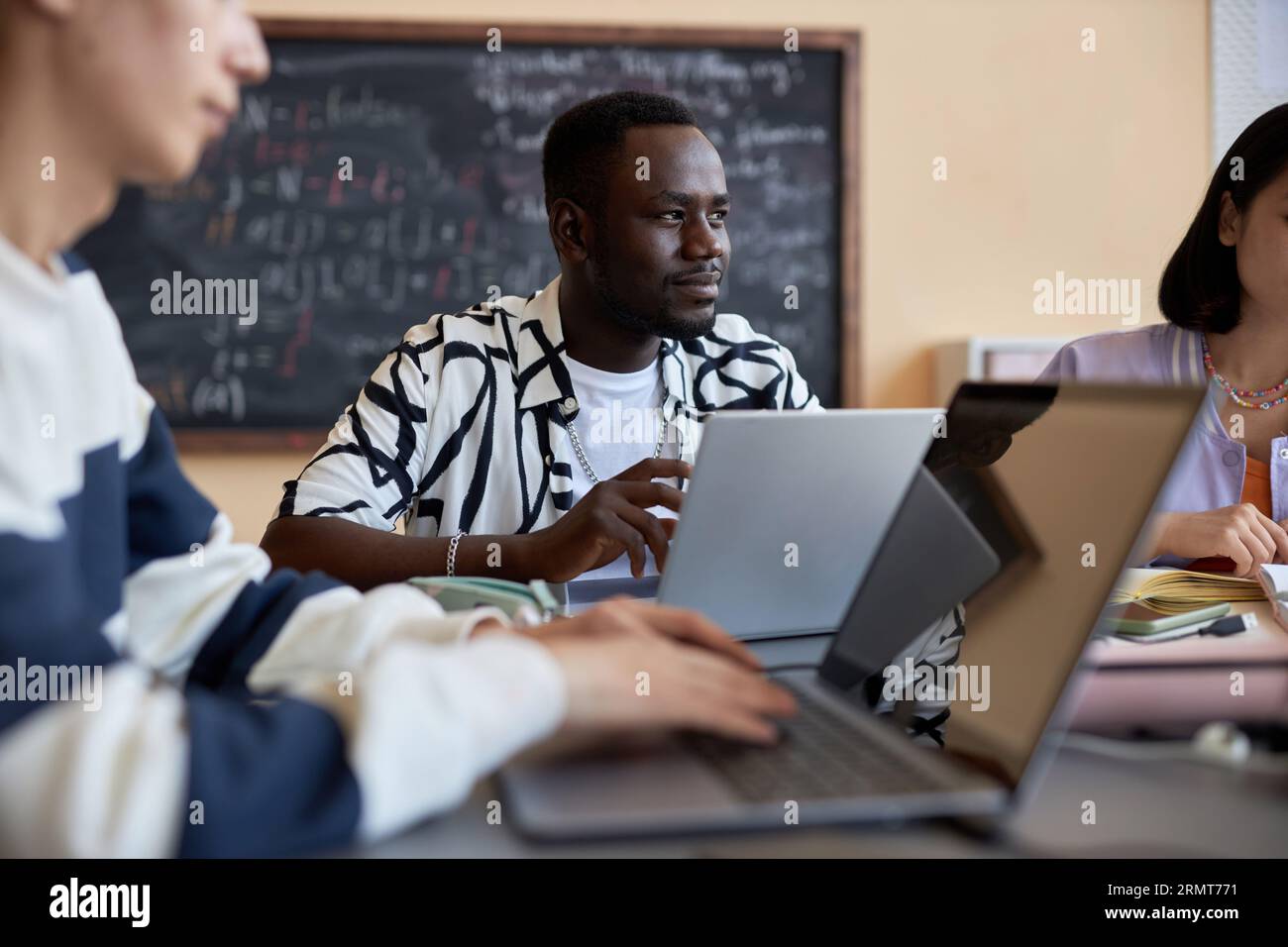 Young pensive male student sitting in front of laptop next to female classmate while working ...