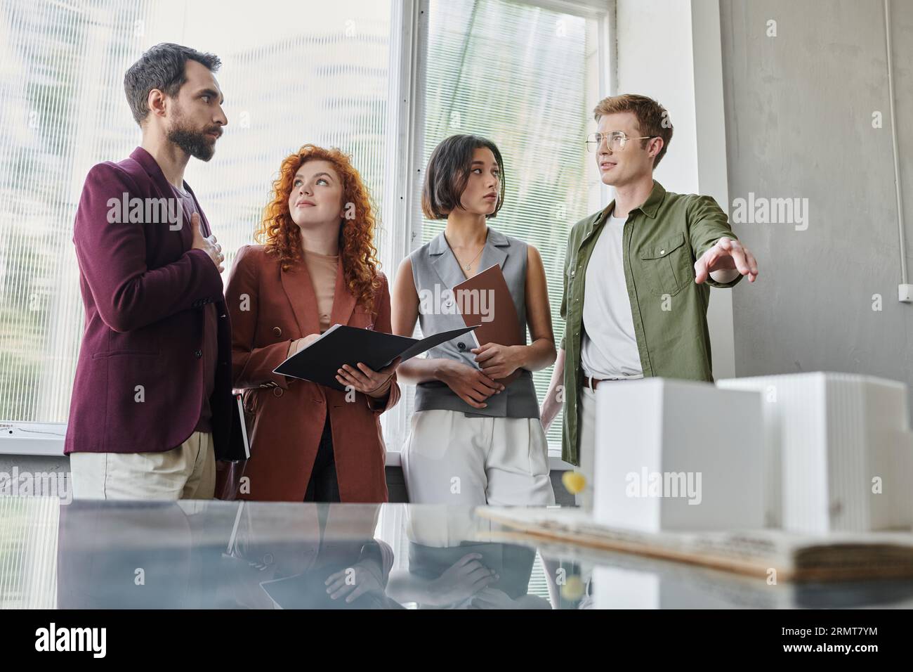 young designer talking to investors and pointing at building model ...