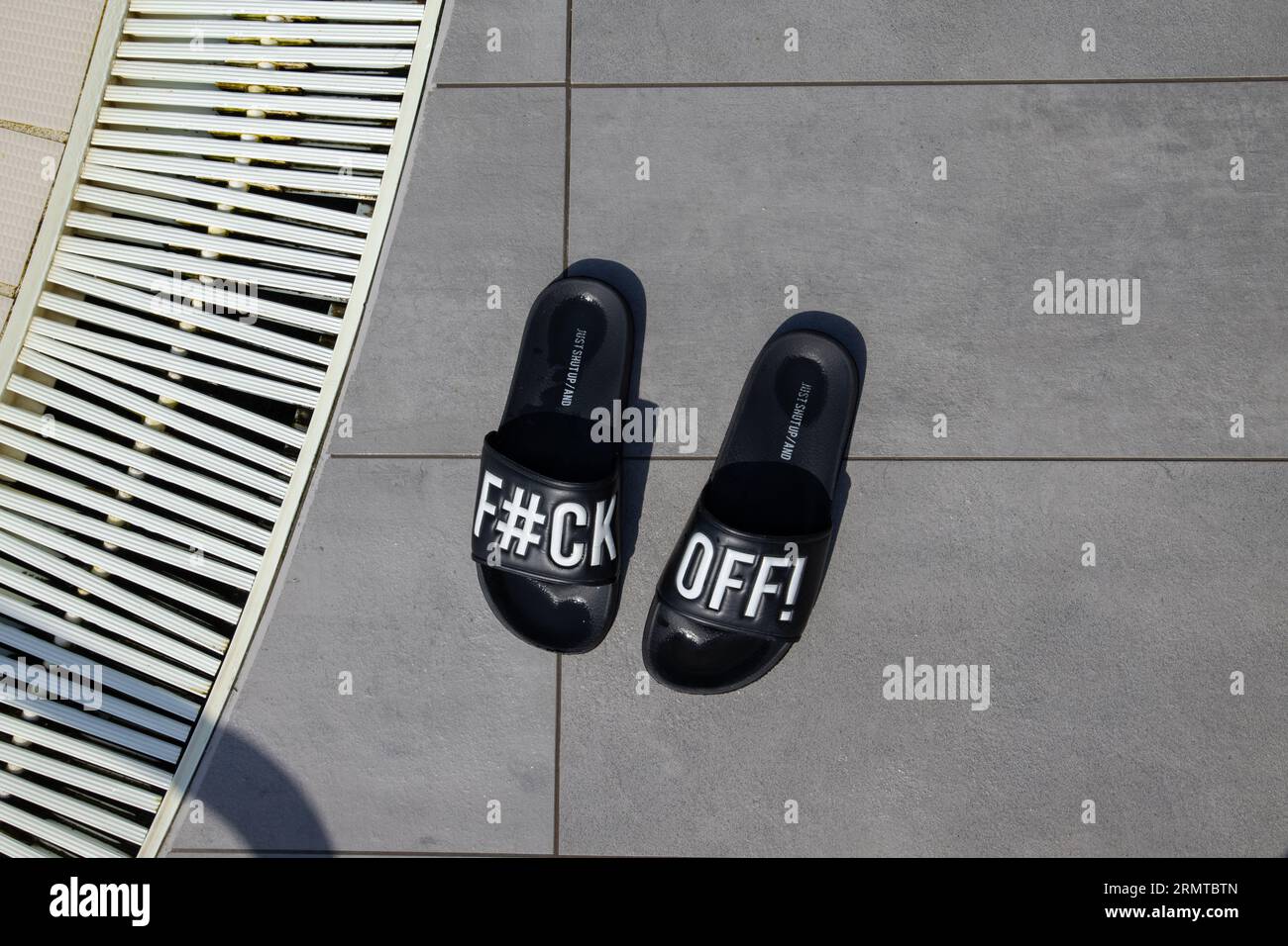 Swimming pool sandals with a distinctive rude message left next to a swimming pool at a european ...