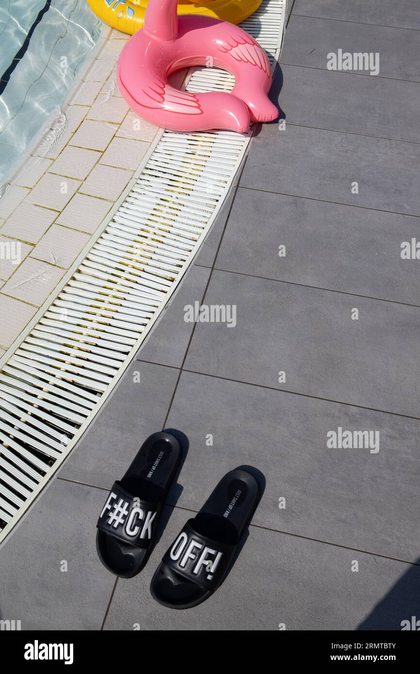 Swimming pool sandals with a distinctive rude message left next to a swimming pool at a european ...