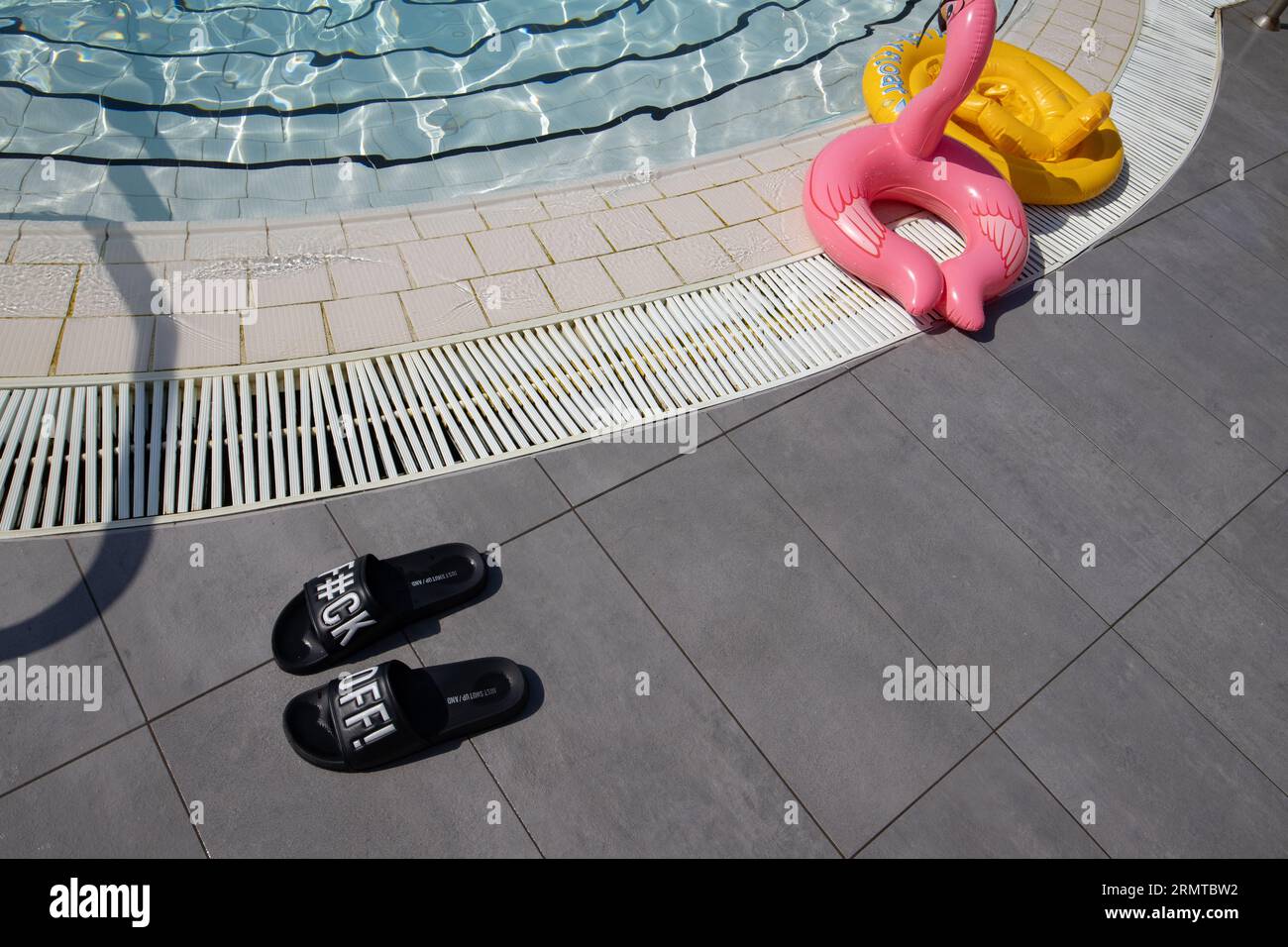 Swimming pool sandals with a distinctive rude message left next to a swimming pool at a european ...