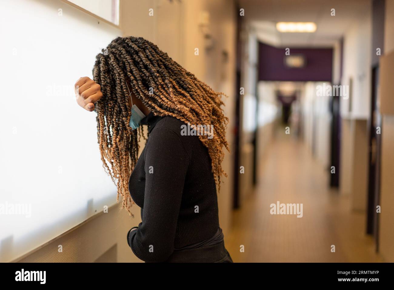 A young female with dreadlocks wearing a face covering leaning on a ...