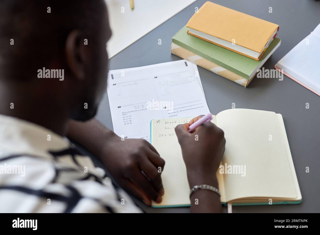 Close-up of young black man writing down formula or equation on page of ...