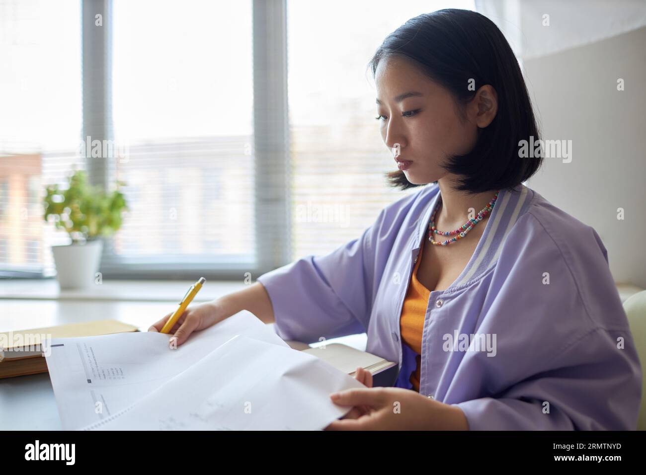 Young Asian woman in casualwear looking through papers with test ...