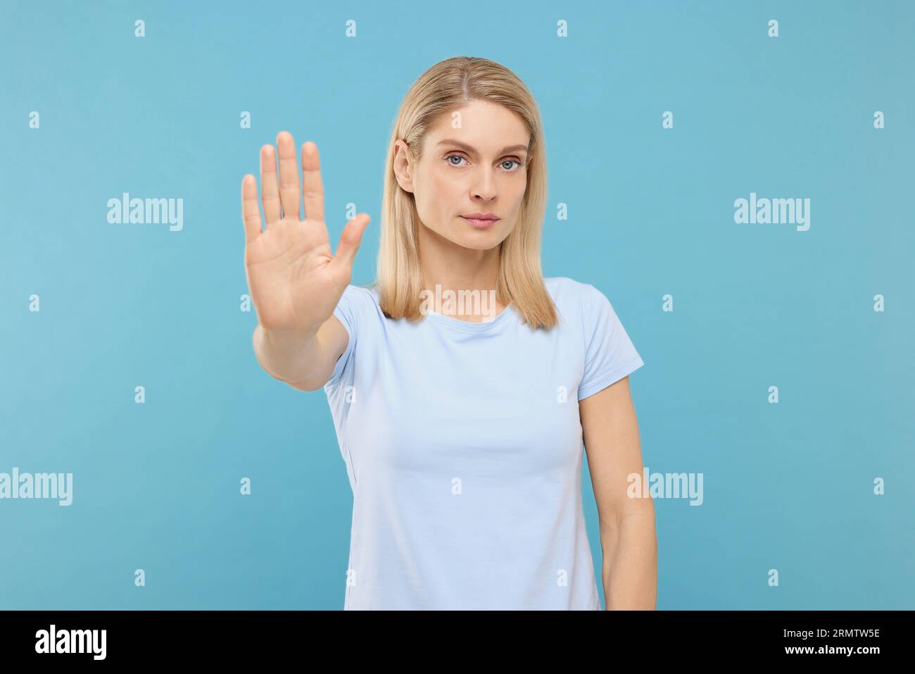 Woman showing stop gesture on light blue background Stock Photo - Alamy