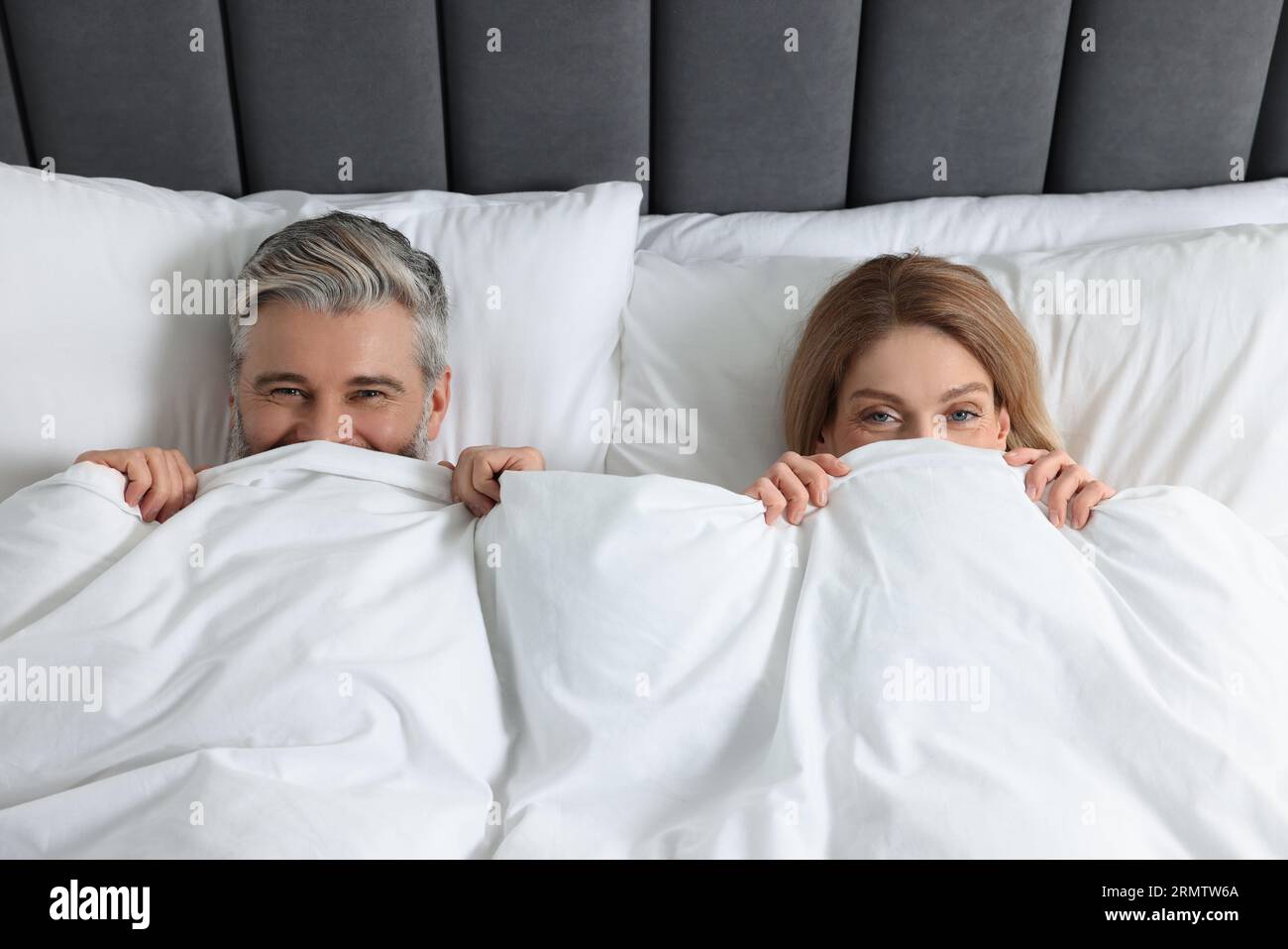 Lovely mature couple hiding together under blanket in bed at home ...