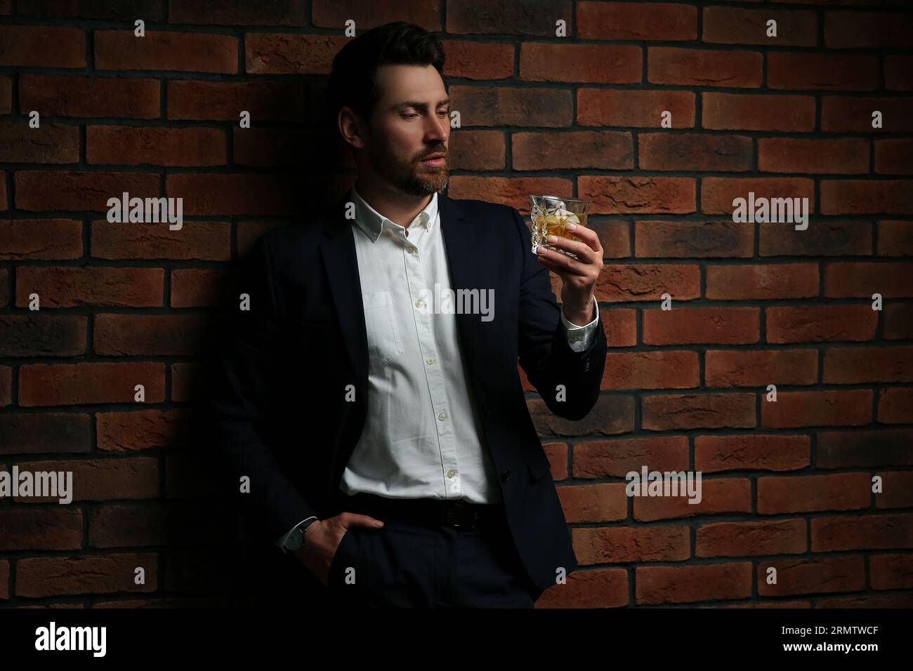 Man in formal suit holding glass of whiskey near red brick wall Stock ...