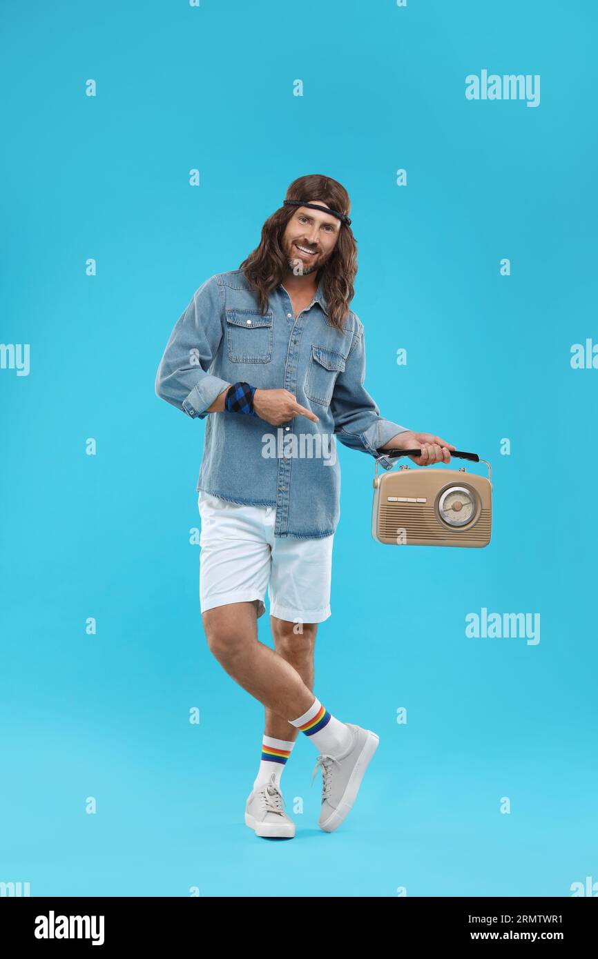 Stylish hippie man pointing at retro radio receiver on light blue ...