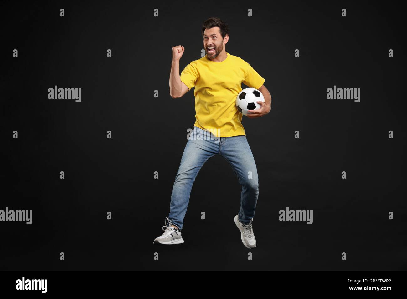Emotional sports fan with soccer ball jumping on black background Stock ...