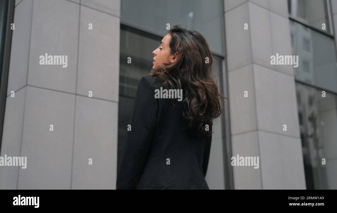 Woman Caucasian with long dark hair and black suit turning to the ...