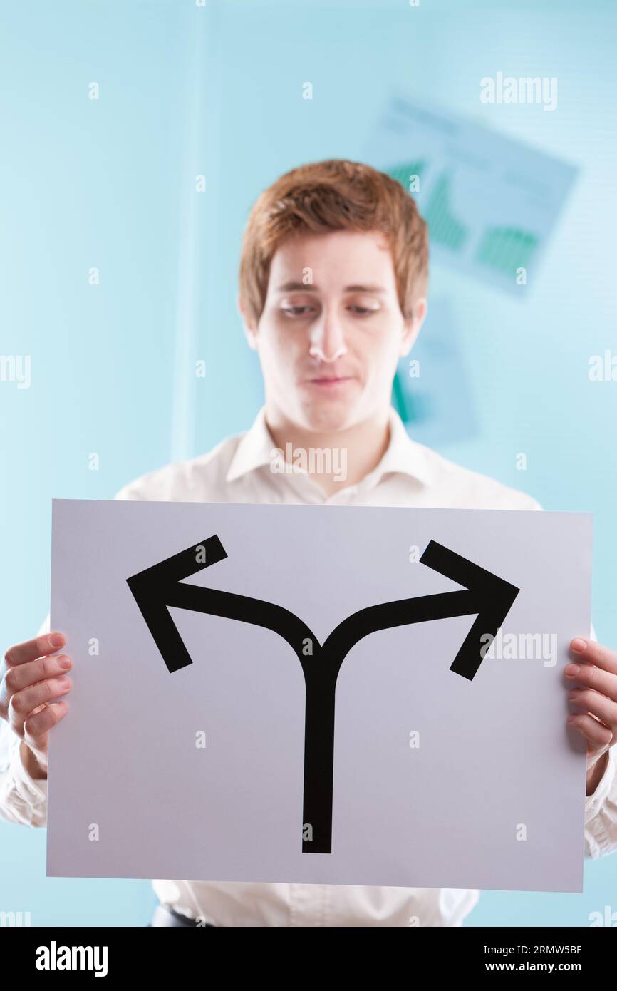 Young man, business backdrop, presents an arrow-sign stopping at a ...