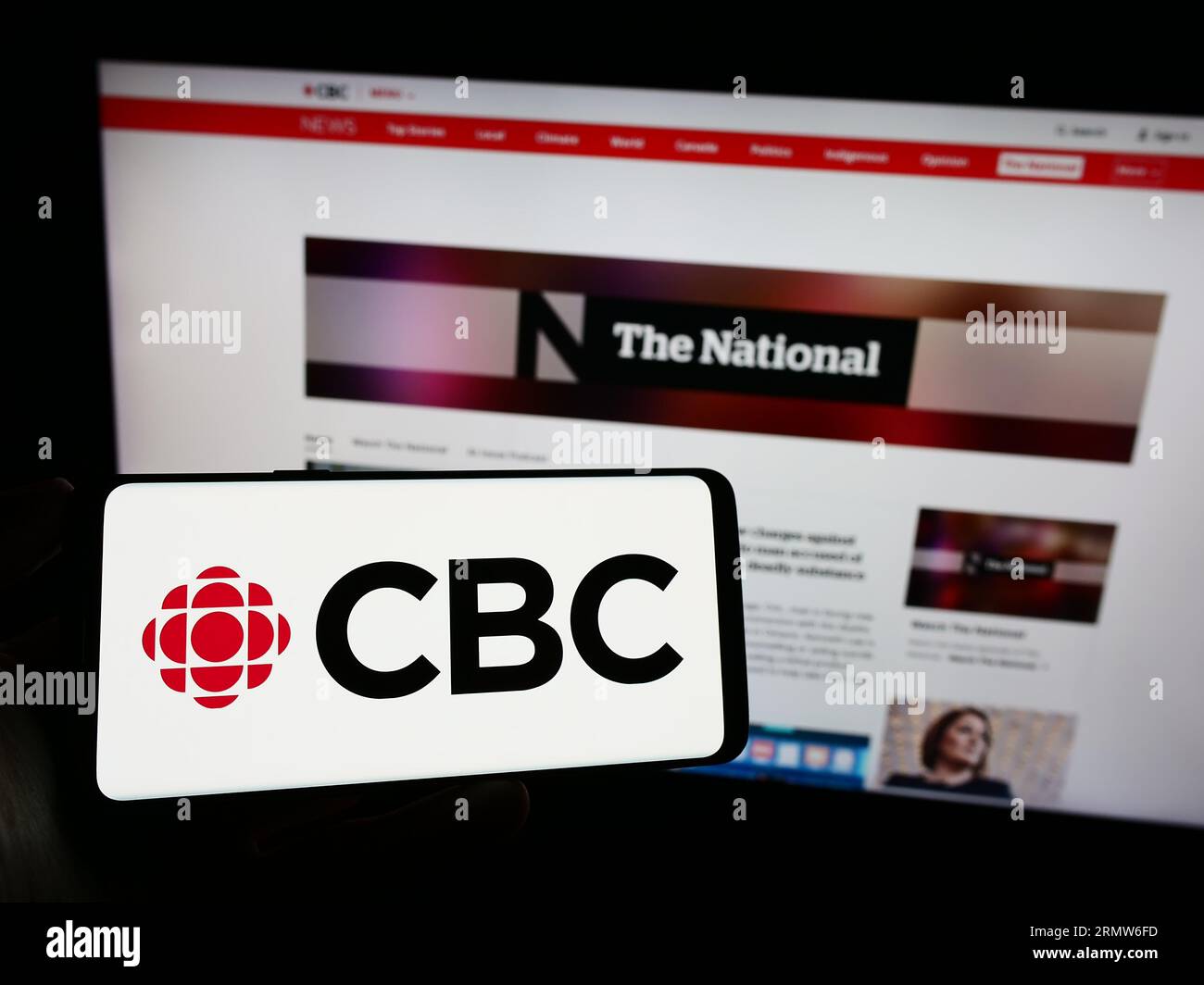 Person holding mobile phone with logo of Canadian Broadcasting Corporation (CBC) on screen in ...