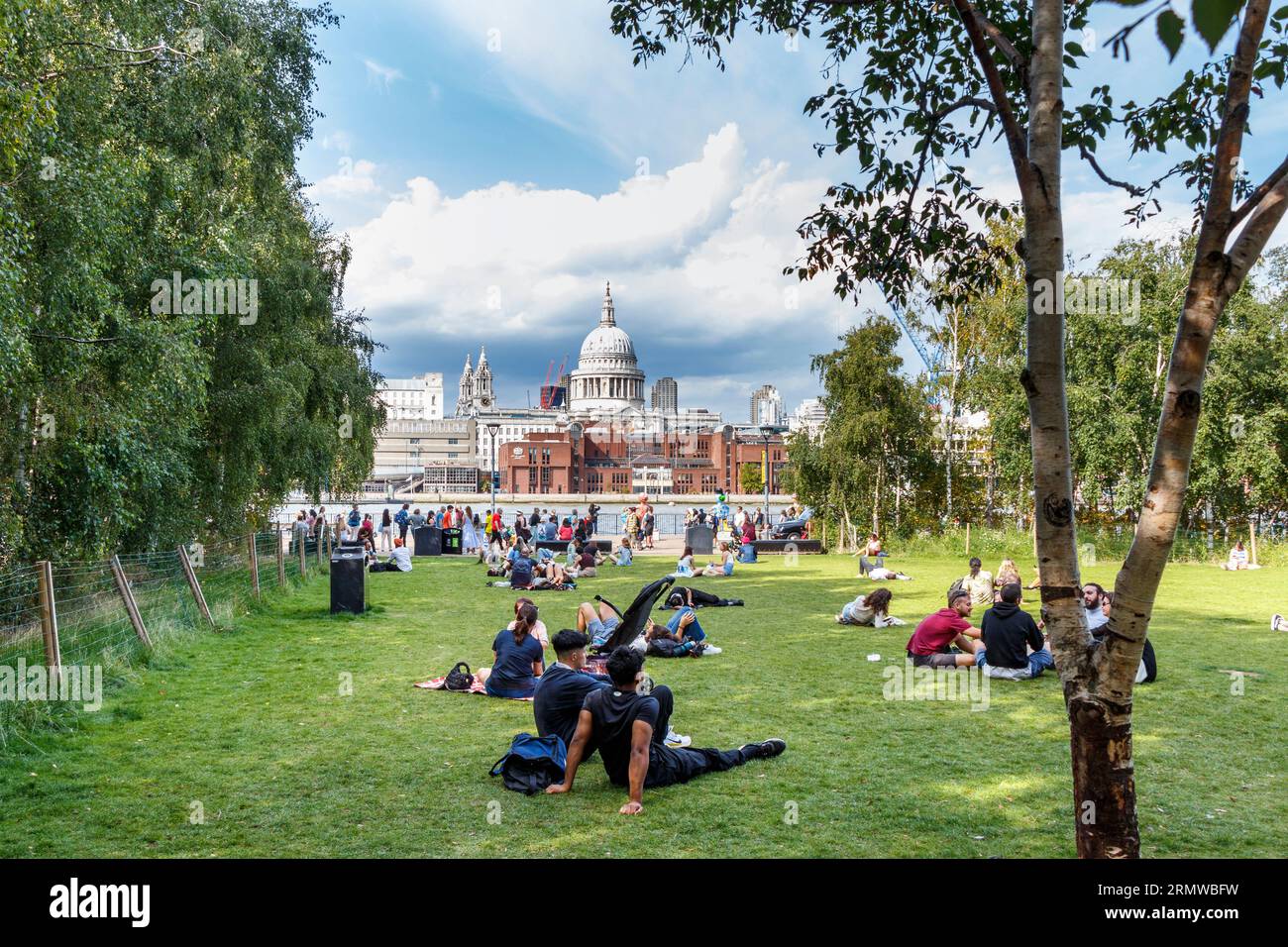 People enjoying the sun in a grassy area by the River Thames at ...