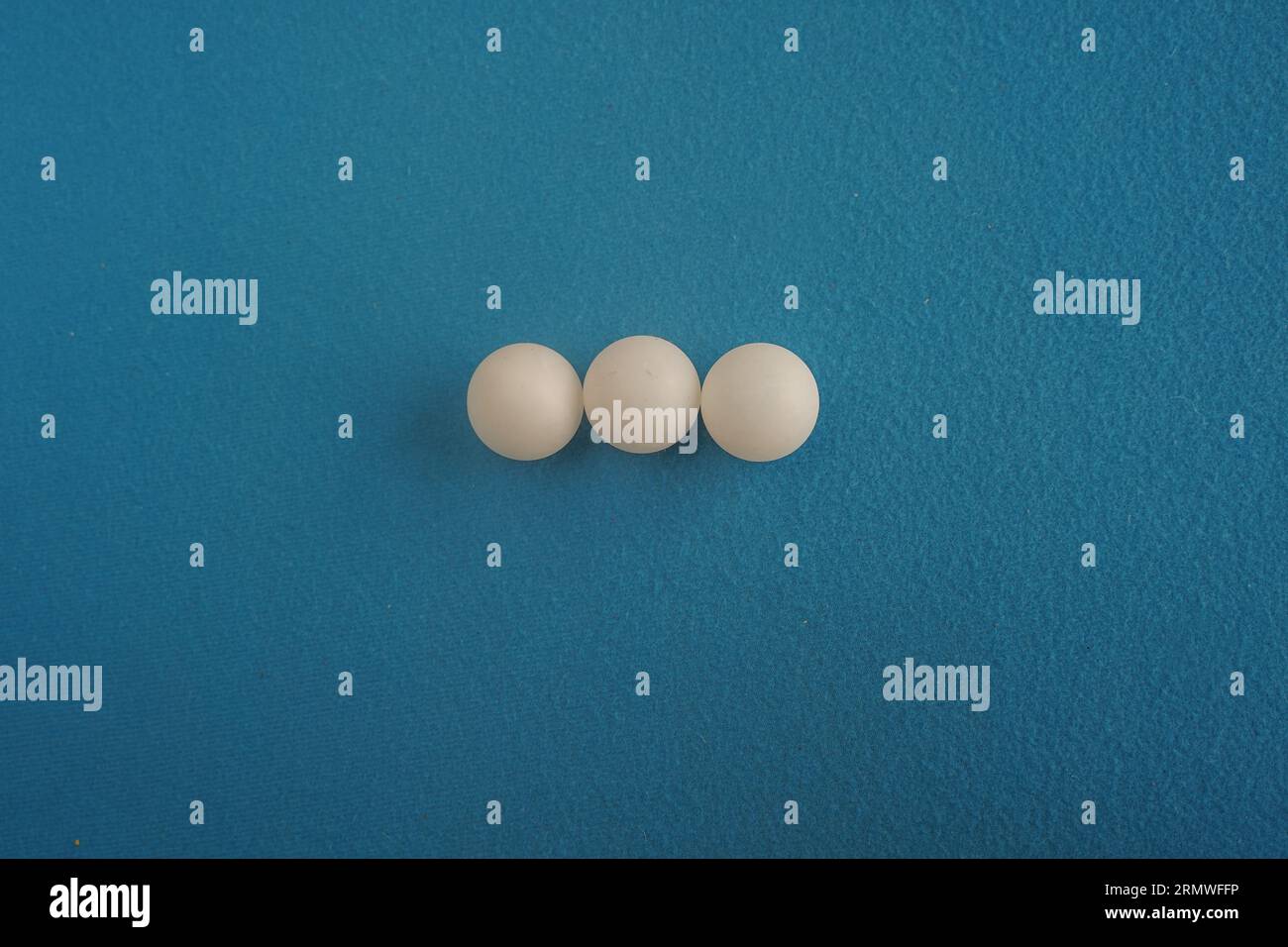 Three ping pong or table tennis balls lie in a row on a blue background ...