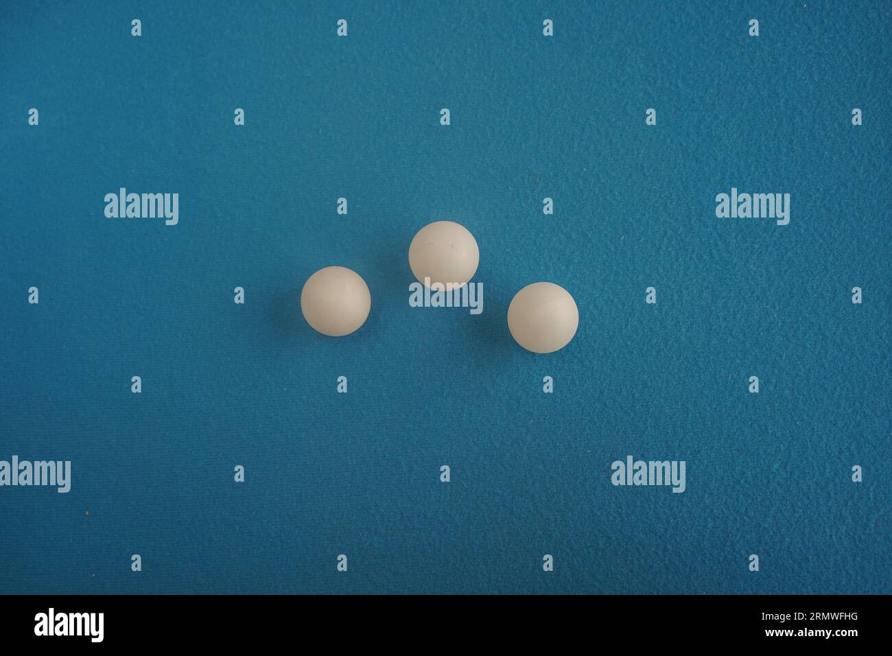 Three ping pong tennis balls lie in a row on a blue background with a ...