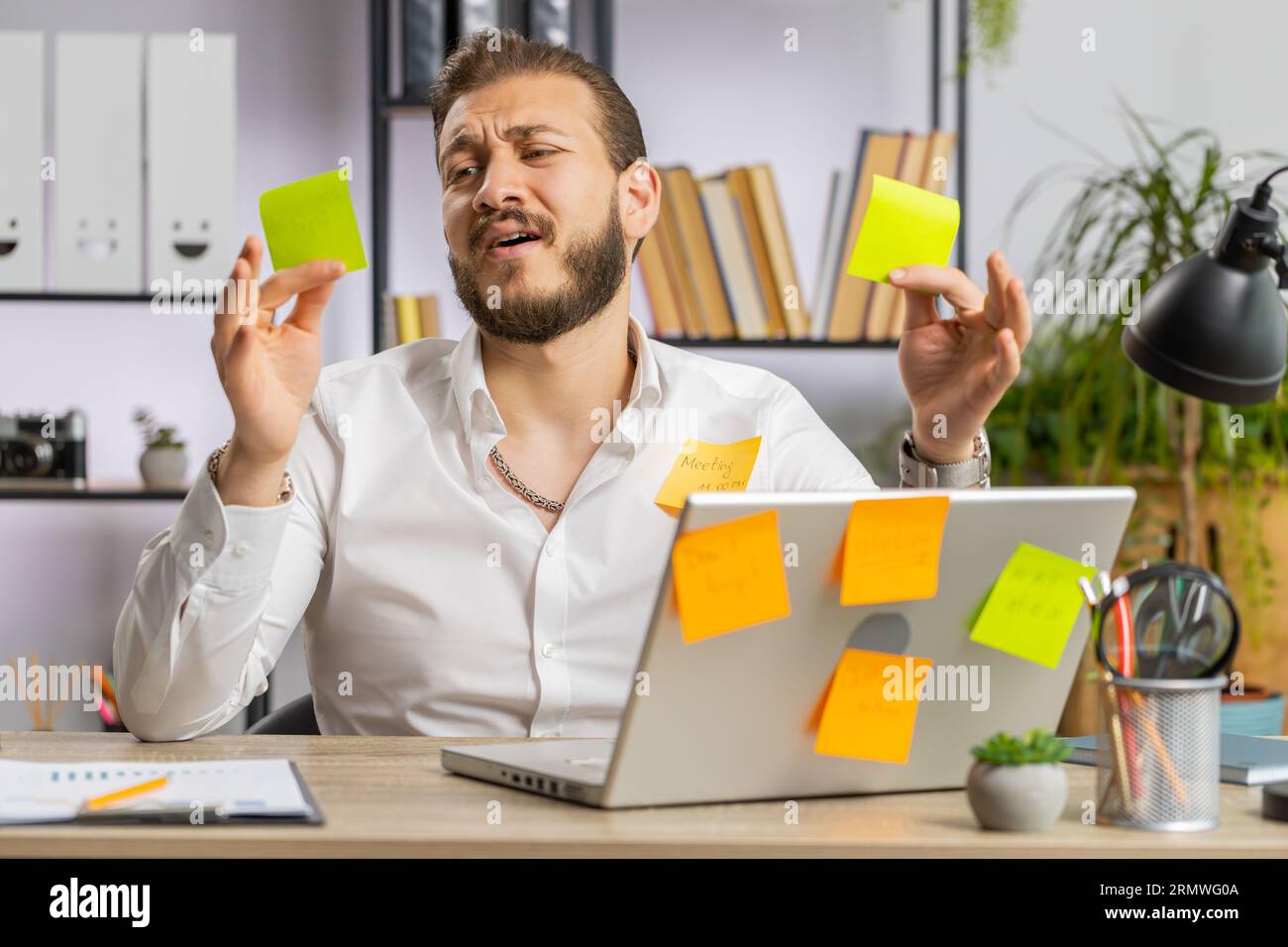 Tired exhausted young businessman working on laptop at office with many ...