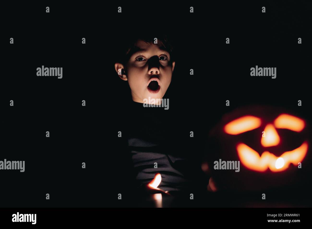 Little boys making scary face in darkness by light og jack-o-lantern ...