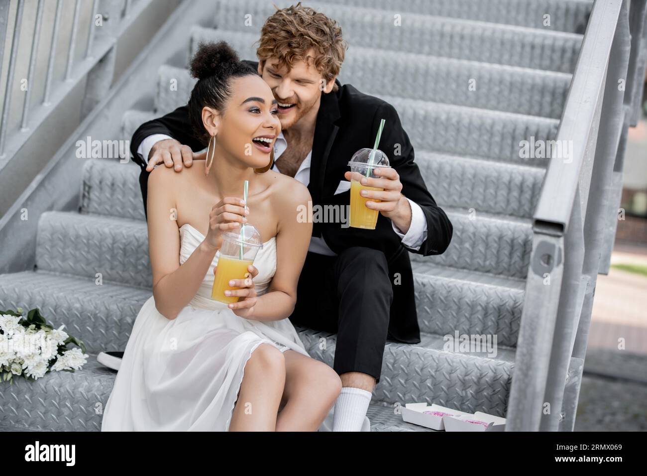 excited african american bride with orange juice laughing near groom on ...