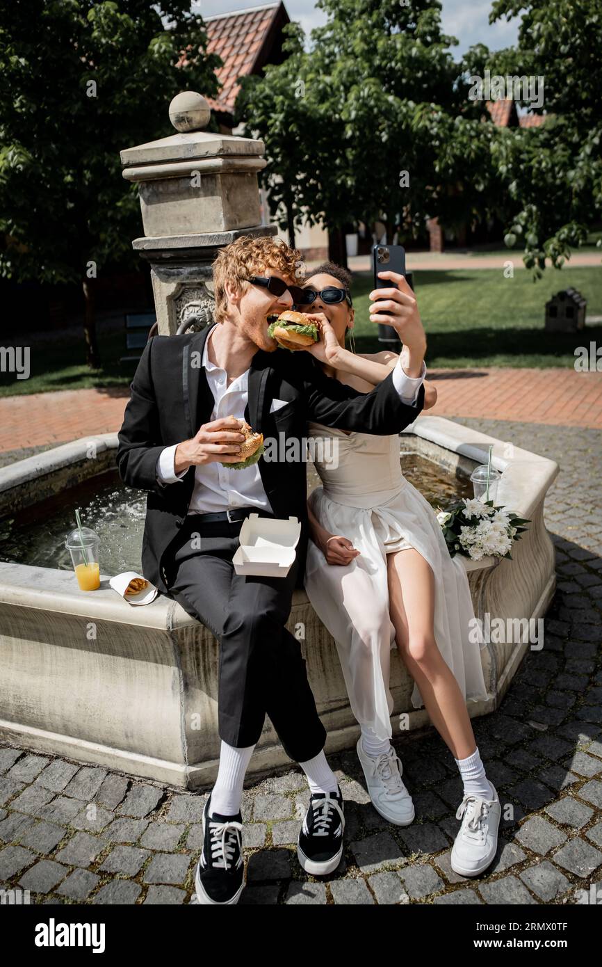 african american woman with burger feeding groom taking selfie on ...