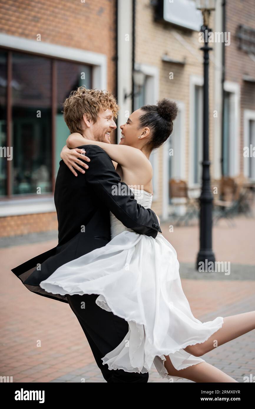 Interracial Couple In Wedding Attire Embracing On City Street