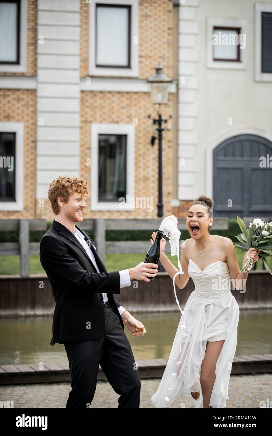 excited african american bride near groom with champagne pouring from ...