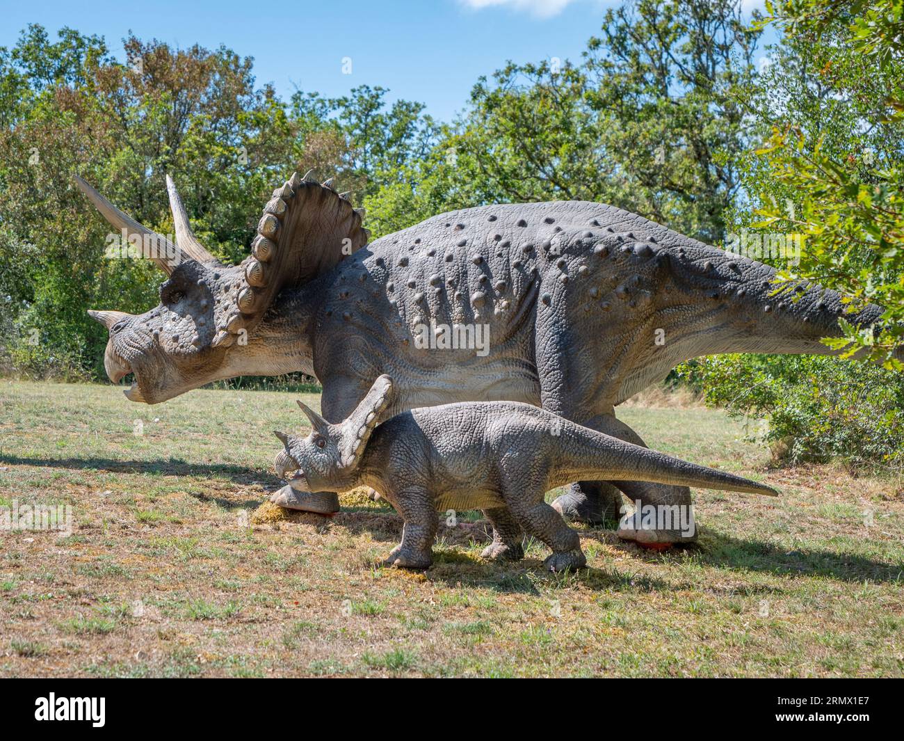 Two life-sized replica dinosaur sculptures standing in a green park in ...