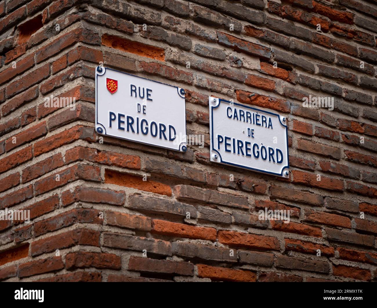 This image shows a red brick building wall with two signs attached ...
