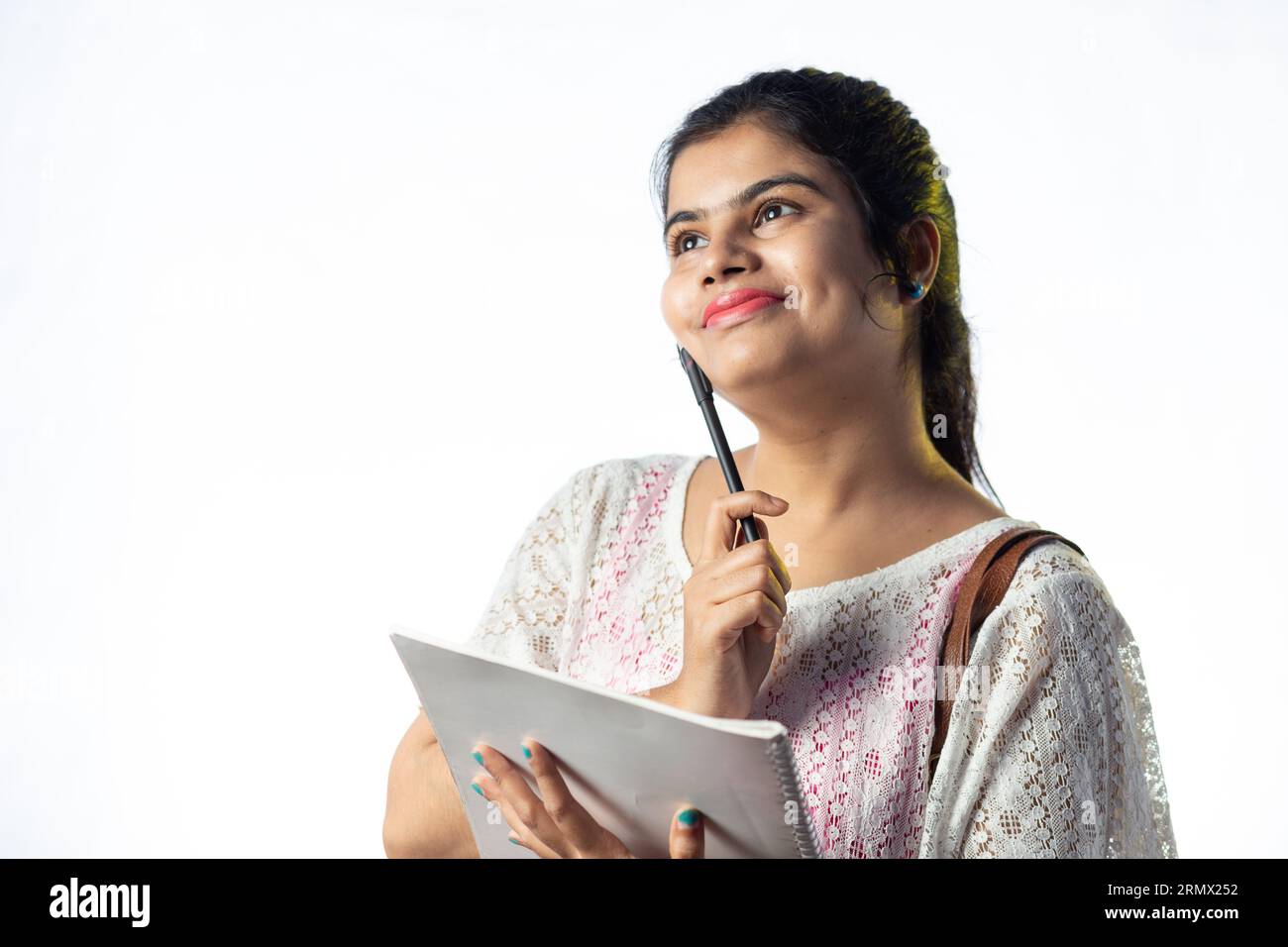 A pretty young Indian girl thinking and taking notes on white ...