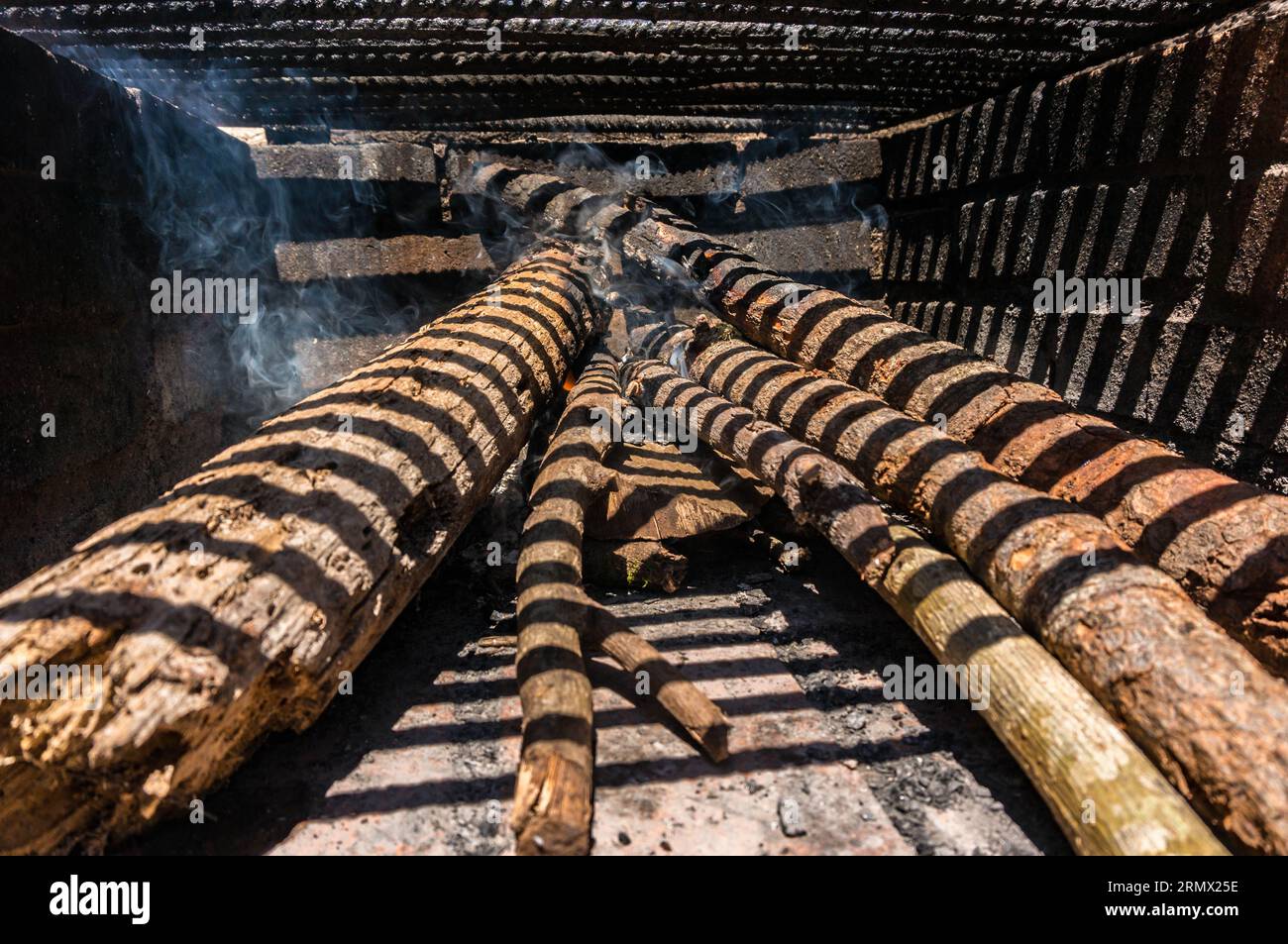 Barbecue wood logs giving smoke and about to catch fire. Striped shadow ...