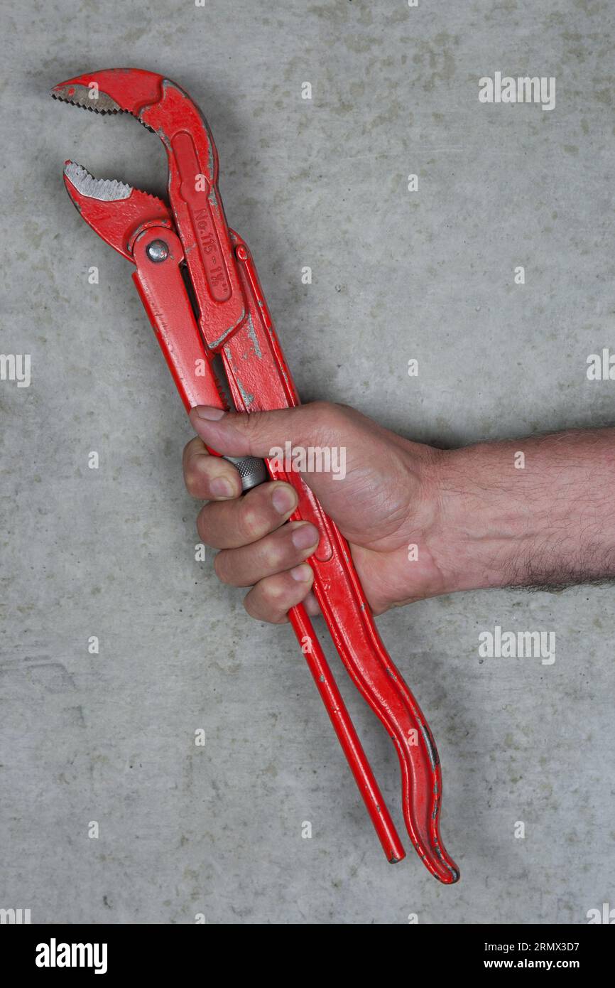 Red pipe wrench in the craftsman's fist. Concentrated power of ...