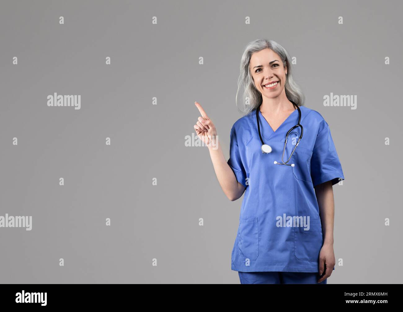 Positive nurse doctor lady in blue workwear pointing aside, studio ...