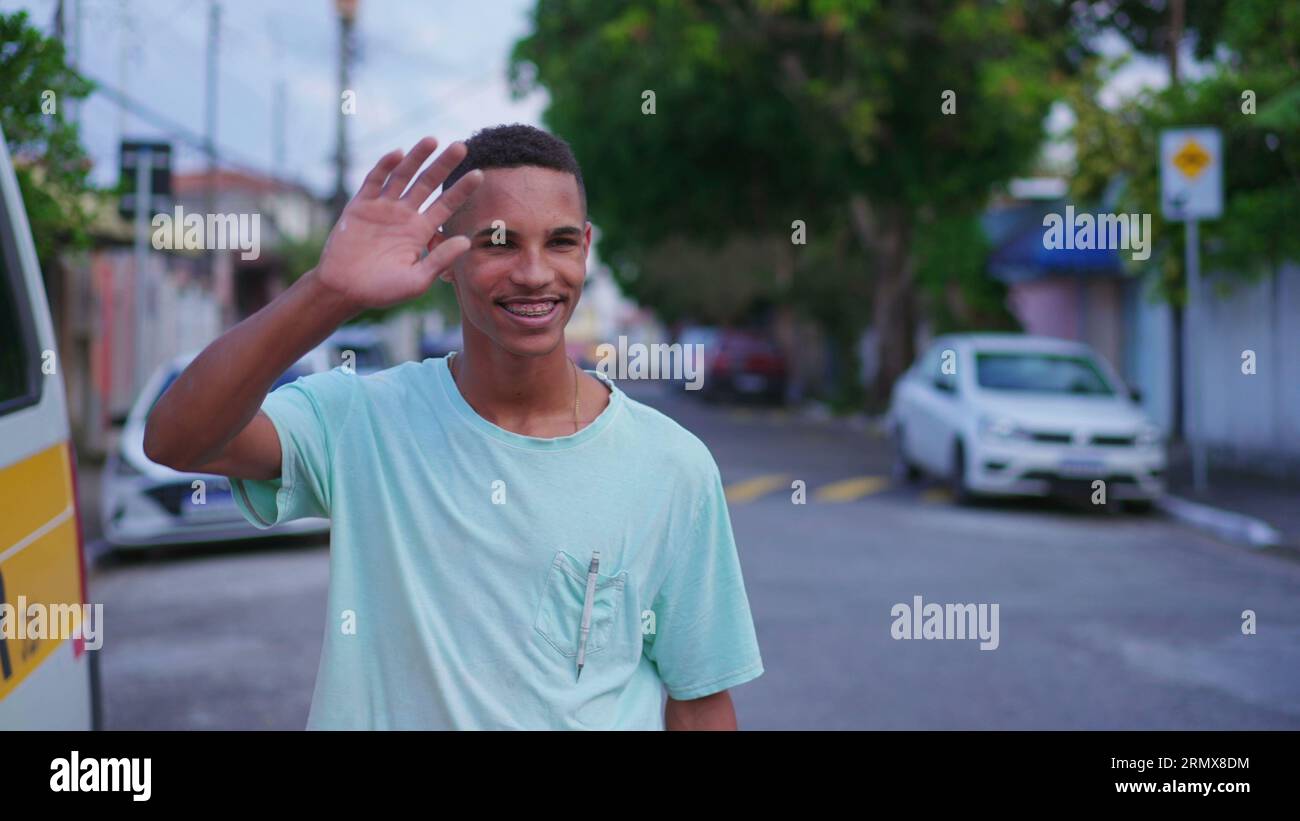 One cheerful young Brazilian man waving hello to neighbor walking in ...