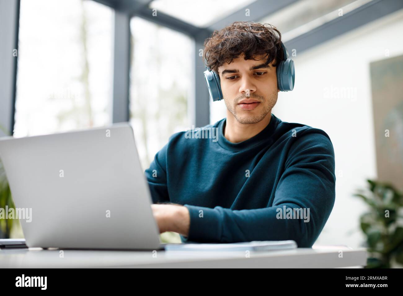 Focused guy student in wireless headphones using laptop and checking ...