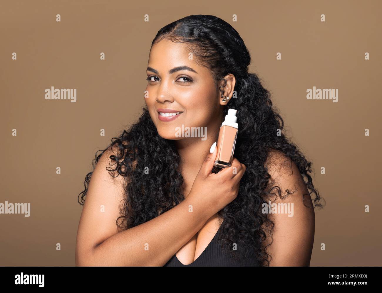 Glad latin body positive lady enjoying base nature makeup, showing foundation, posing on brown ...