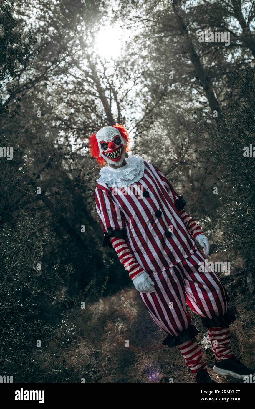 a mad evil redhead clown, wearing a white and red striped costume with ...