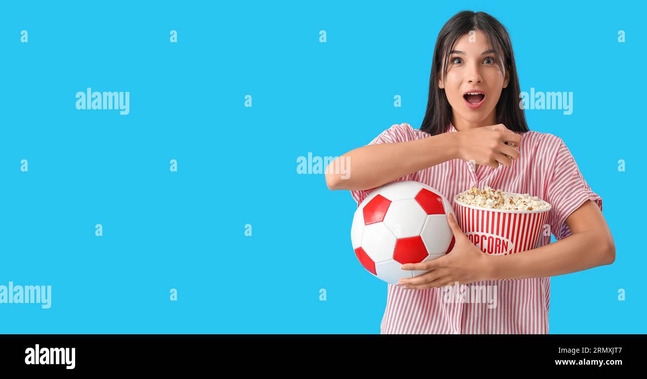 Shocked female soccer fan with popcorn and ball on blue background with ...