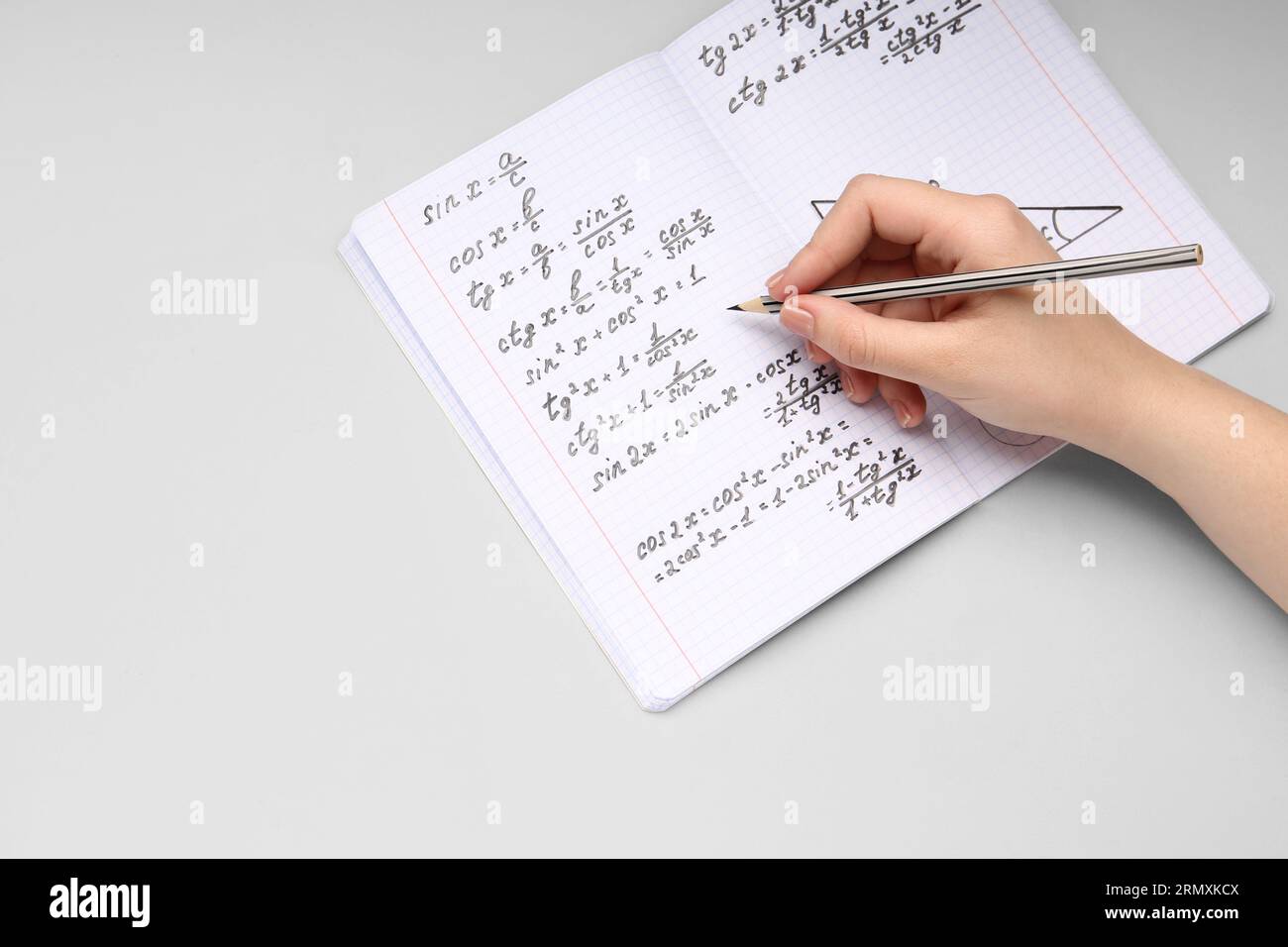 Woman writing maths formulas in copybook with pencil on grey background ...