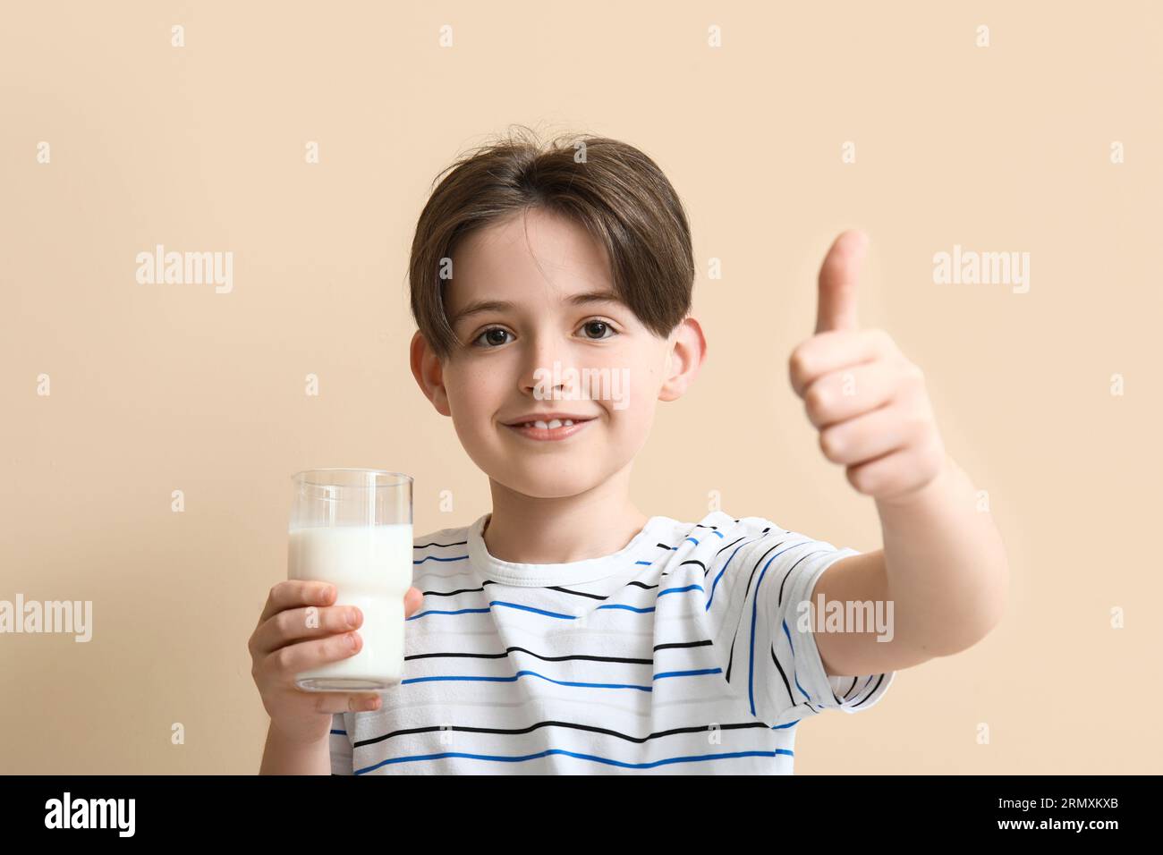 Little boy with glass of milk showing thumb-up gesture on beige ...