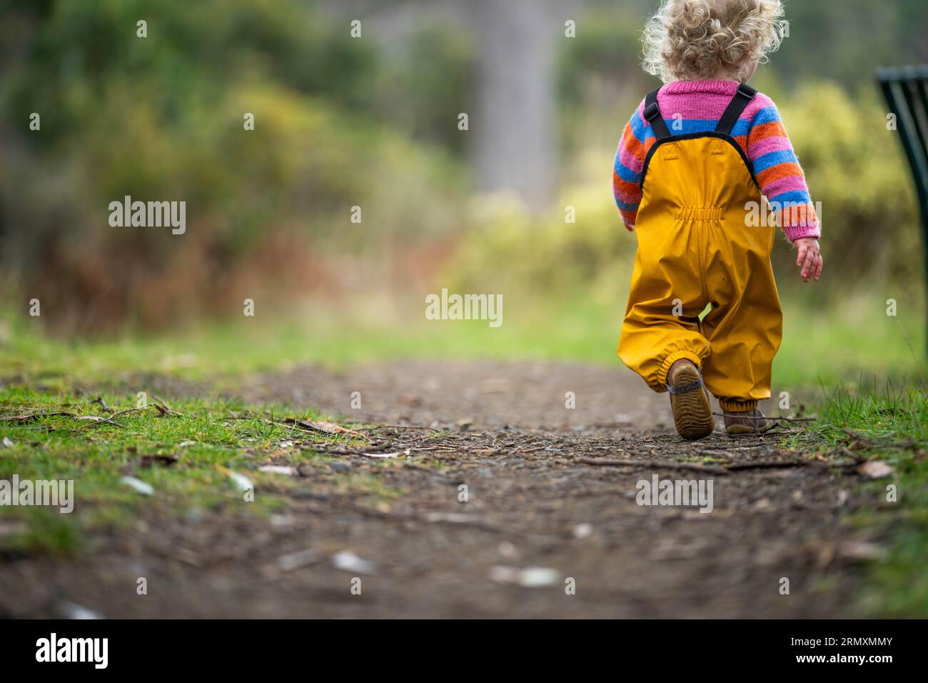 baby running down a path in yellow overalls in the bush Stock Photo - Alamy