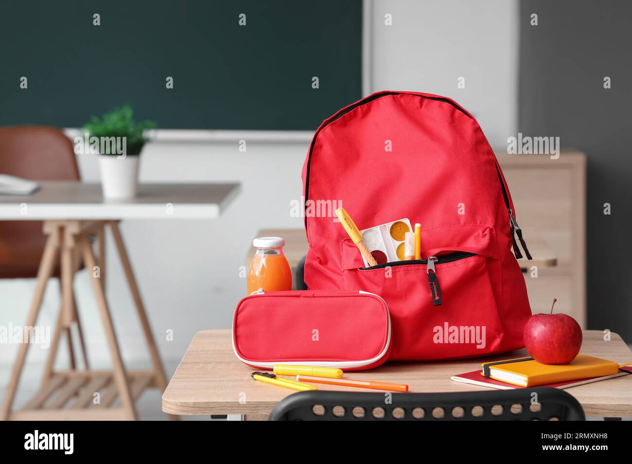 Red school backpack with stationery and lunch on desk in classroom ...