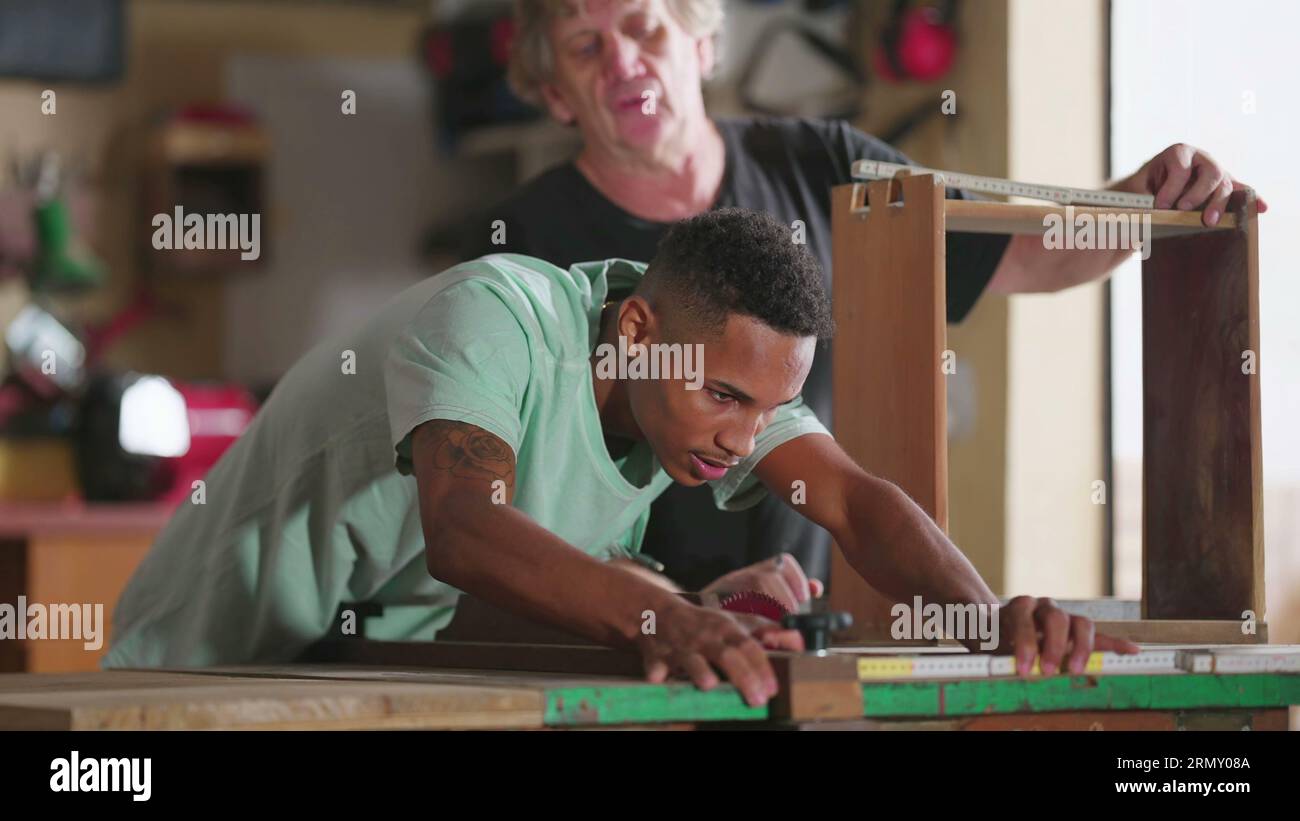Candid scene of carpenters working at workshop, a young black pupil ...