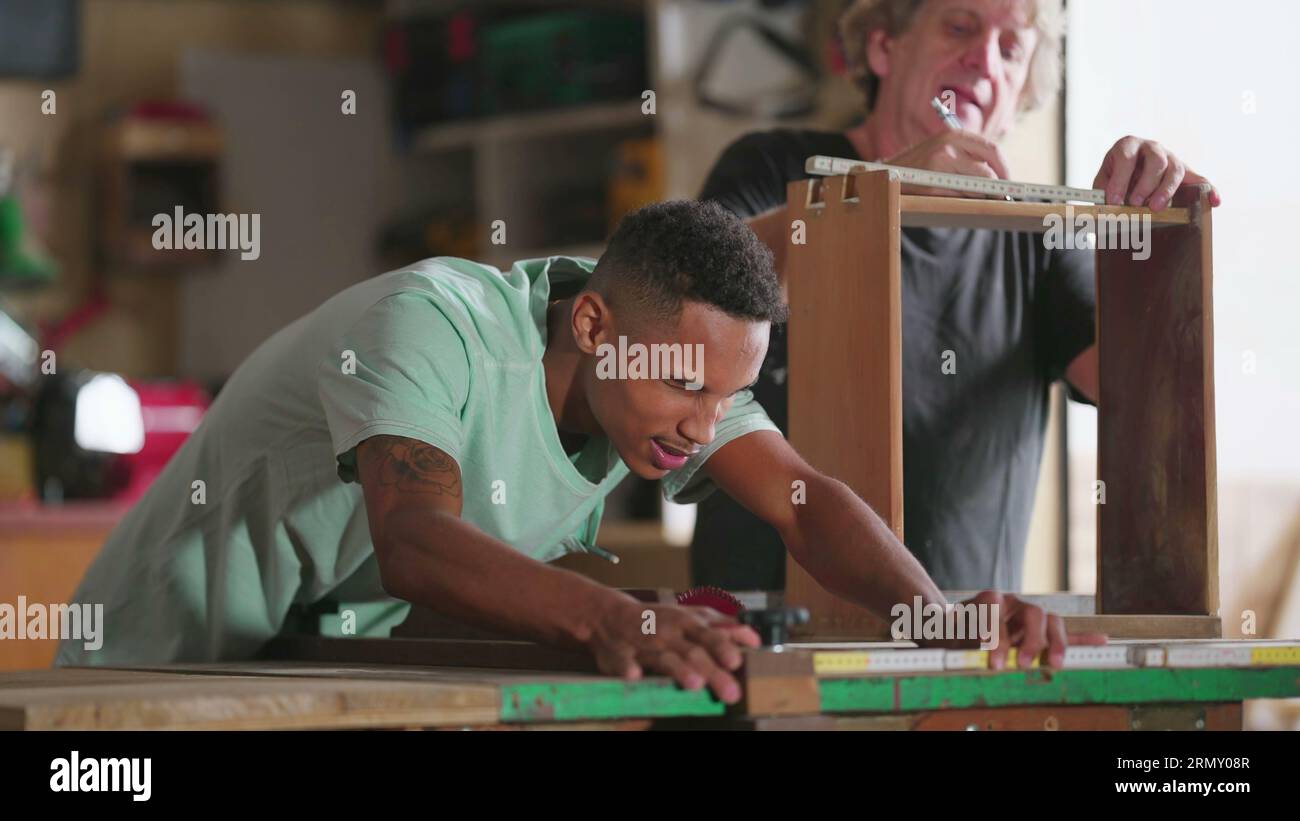 Candid scene of carpenters working at workshop, a young black pupil ...