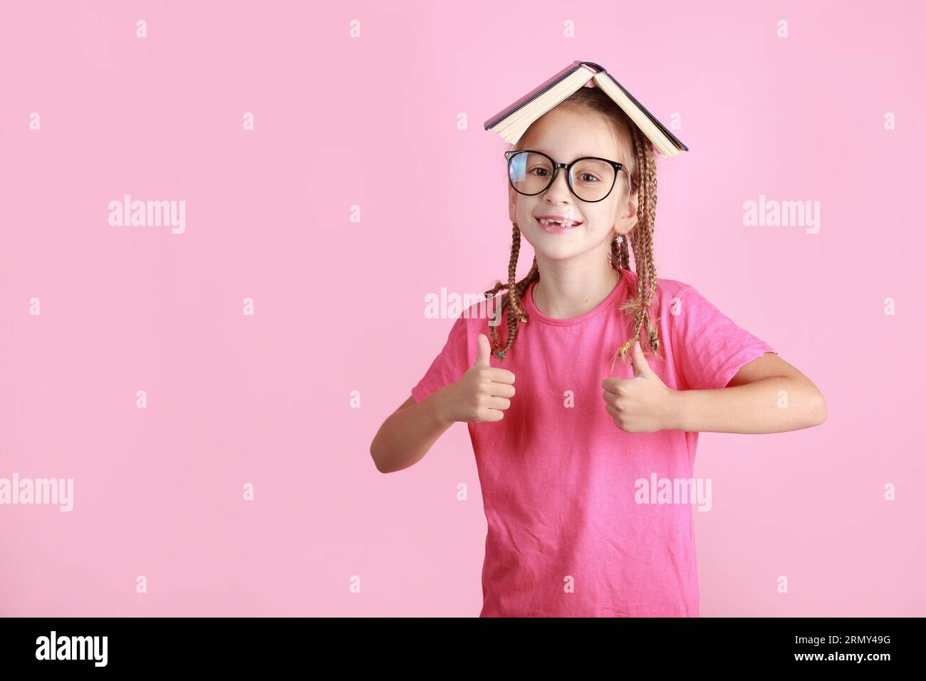 Back to school concept. Smiling pretty little school girl in glasses is holding book over head ...