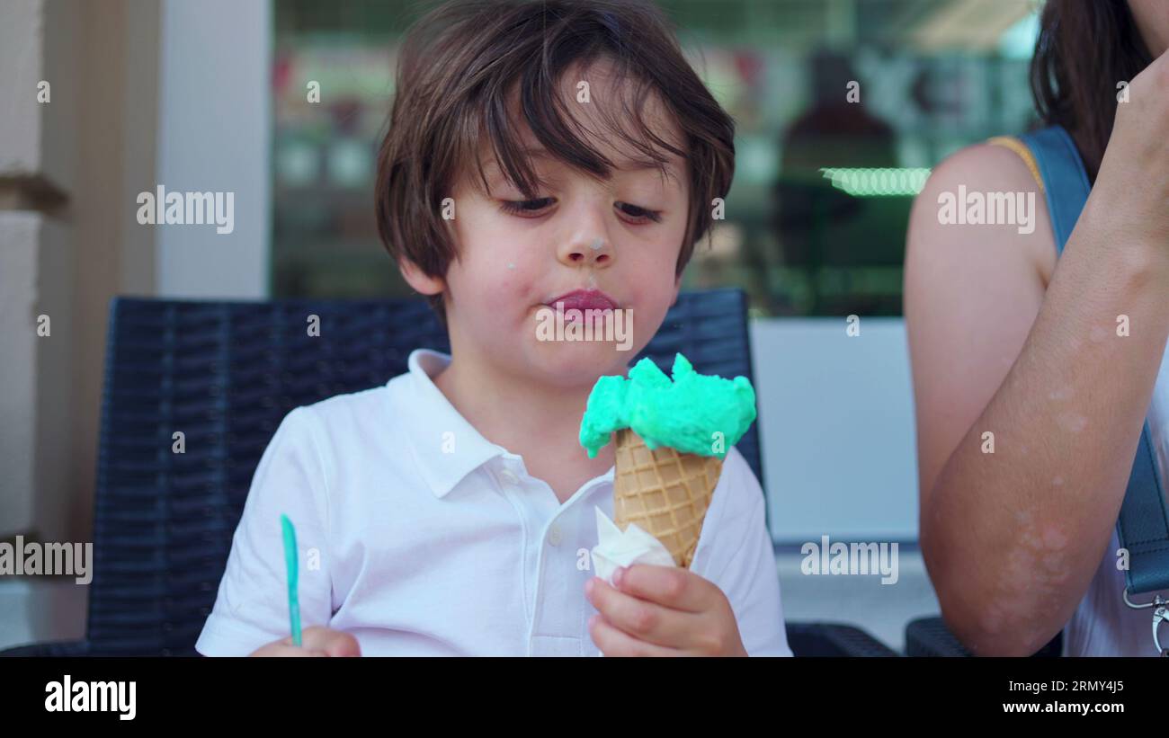 Child enjoying ice-cream cone at parlo shop during summer day. Mother ...