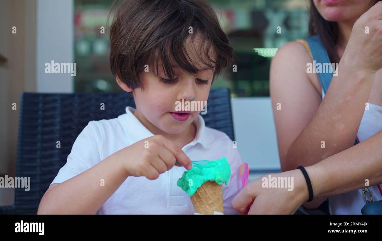 Child enjoying ice-cream cone at parlo shop during summer day. Mother ...