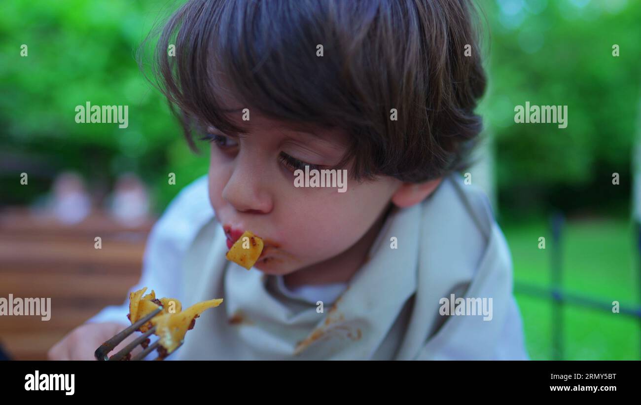 Messy small boy eating pasta for lunch in outdoors sunny setting ...